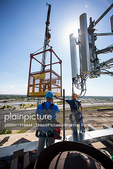 Caucasian workers reaching for basket on cell tower - Stock Image ...