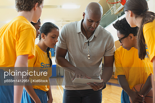 Coach using digital tablet with basketball team during practice in gym ...