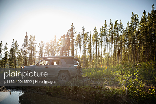 Couple enjoying overland adventure, standing on top of SUV in sunny ...