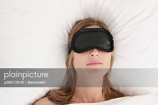 Germany, Woman with eye mask resting on bed - Stock Image - Everypixel
